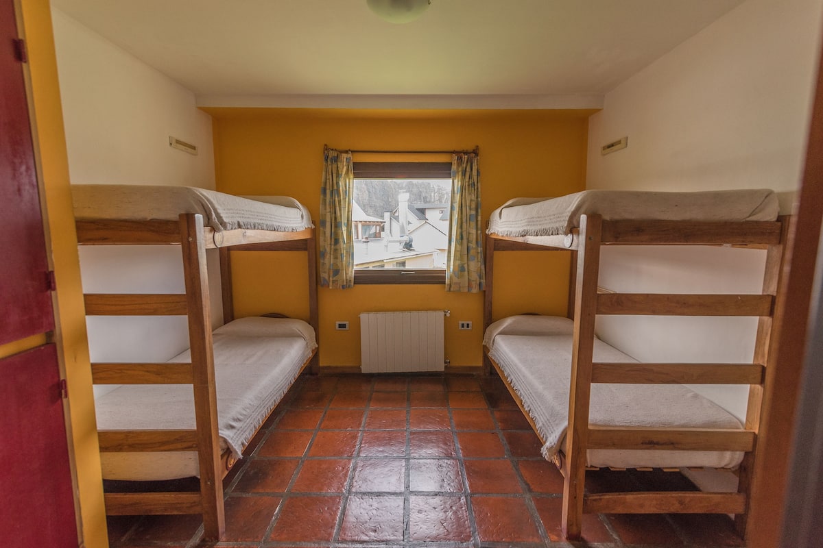 Quarto pequeno e estreito com duas beliches e uma janela com cortinas.