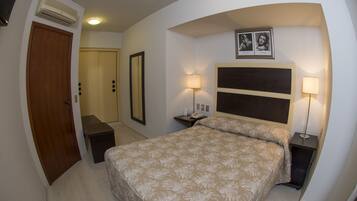 Quarto com uma cama grande, duas mesas de cabeceira com luminárias, um guarda-roupa, um espelho e um ar condicionado.