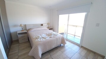 Quarto com cama, mesas de cabeceira, janela e vista para o exterior.