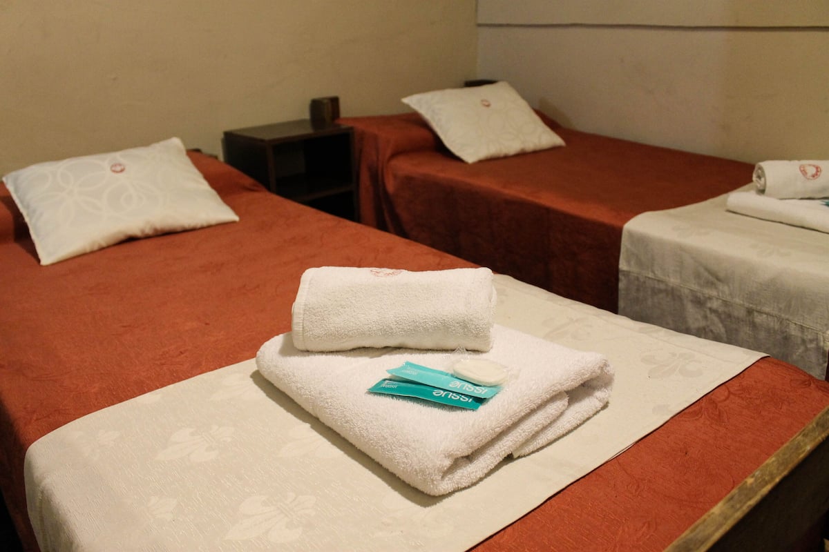 Quarto de hotel com duas camas, cada uma com colcha vermelha e almofadas brancas. Há toalhas e um pequeno cartão na cama em primeiro plano.