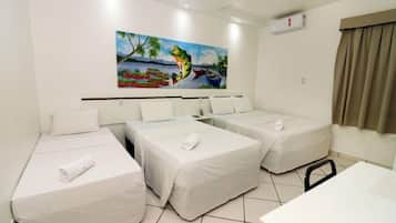 Quarto de hotel com duas camas de solteiro, uma mesa pequena e um quadro de uma paisagem tropical na parede.