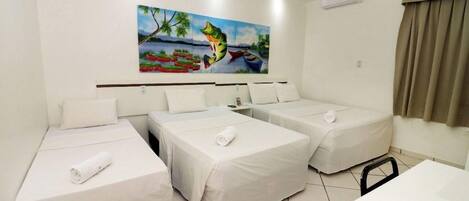 Quarto de hotel com duas camas de solteiro, uma mesa pequena e um quadro de uma paisagem tropical na parede.