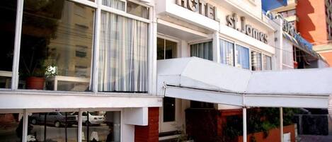 Um hotel com fachada branca, janelas grandes e entrada coberta.