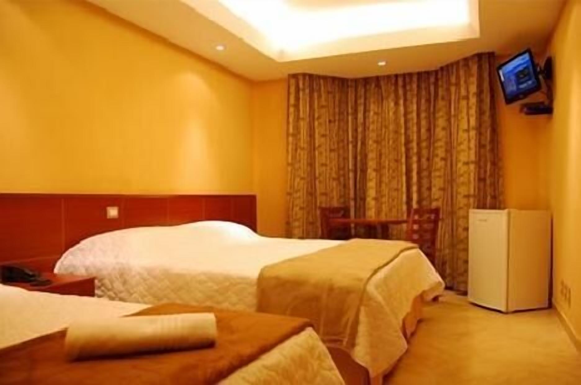 Quarto de hotel com duas camas, uma televisão na parede e uma secretária pequena com uma cadeira.