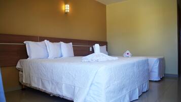 Quarto de hotel com uma cama grande, cabeceira de madeira e luminária fixada na parede.