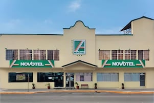 Um hotel com uma placa Novotel bem visível, uma entrada central e uma fachada simétrica com janelas de ambos os lados.