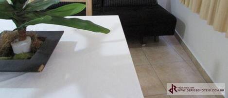 Uma sala de estar moderna com um sofá branco, uma almofada estampada preta e um vaso com folhagem verde exuberante.