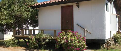 Um pequeno edifício branco com porta marrom e varanda de madeira.