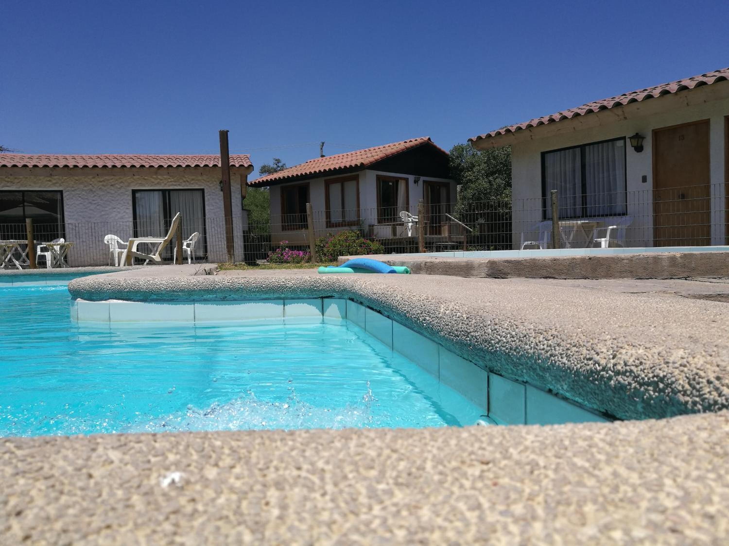 Piscina com borda revestida de pedras, rodeada por edifícios com telhados e janelas.