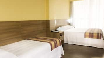 Quarto de hotel com duas camas, cabeceiras de madeira e uma mesinha de cabeceira com telefone.