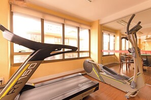 Academia com esteira e máquina elíptica, janelas amplas e espelho refletindo o espaço.