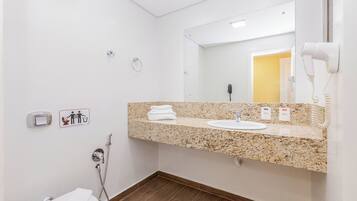 Uma casa de banho moderna com lavatório de bancada em granito, espelho, secador de cabelo e porta-toalhas.
