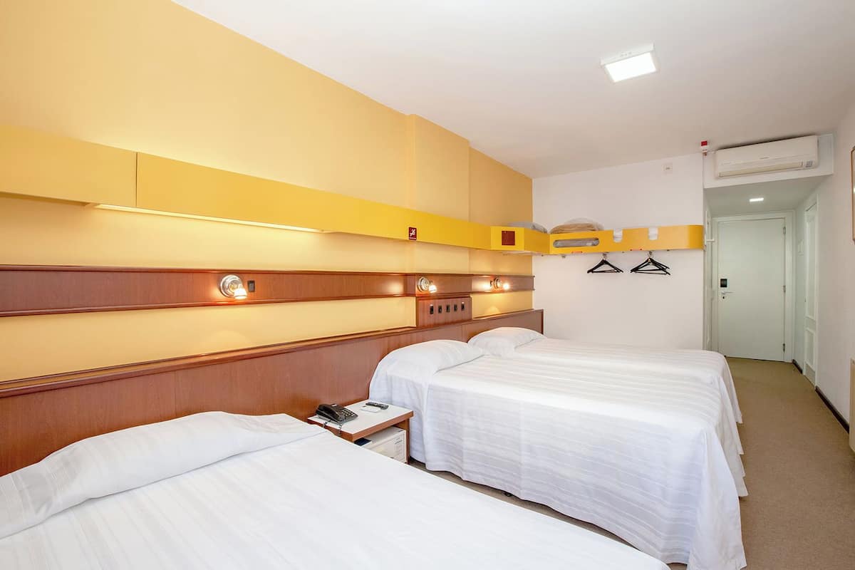 Quarto de hotel com duas camas, uma mesa de cabeceira com telefone e um cabideiro.