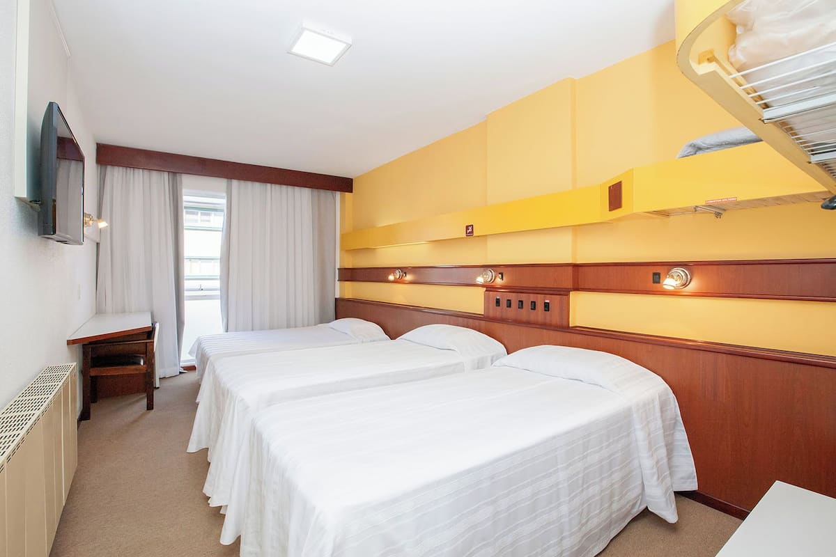 Quarto de hotel com duas camas, uma mesa, uma televisão e uma janela com cortinas.