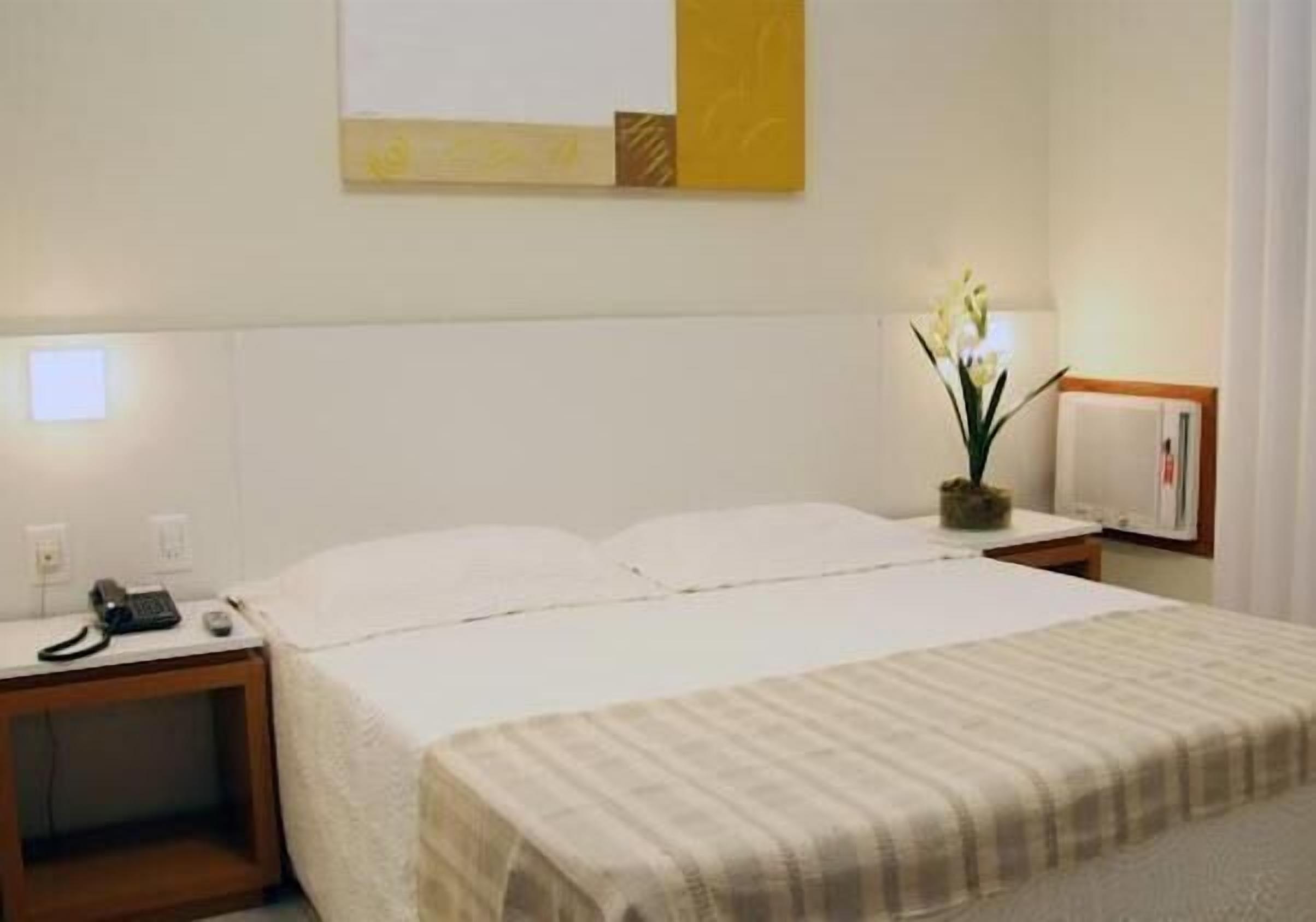 Quarto de hotel com cama, mesa de cabeceira, abajur e uma obra de arte na parede.