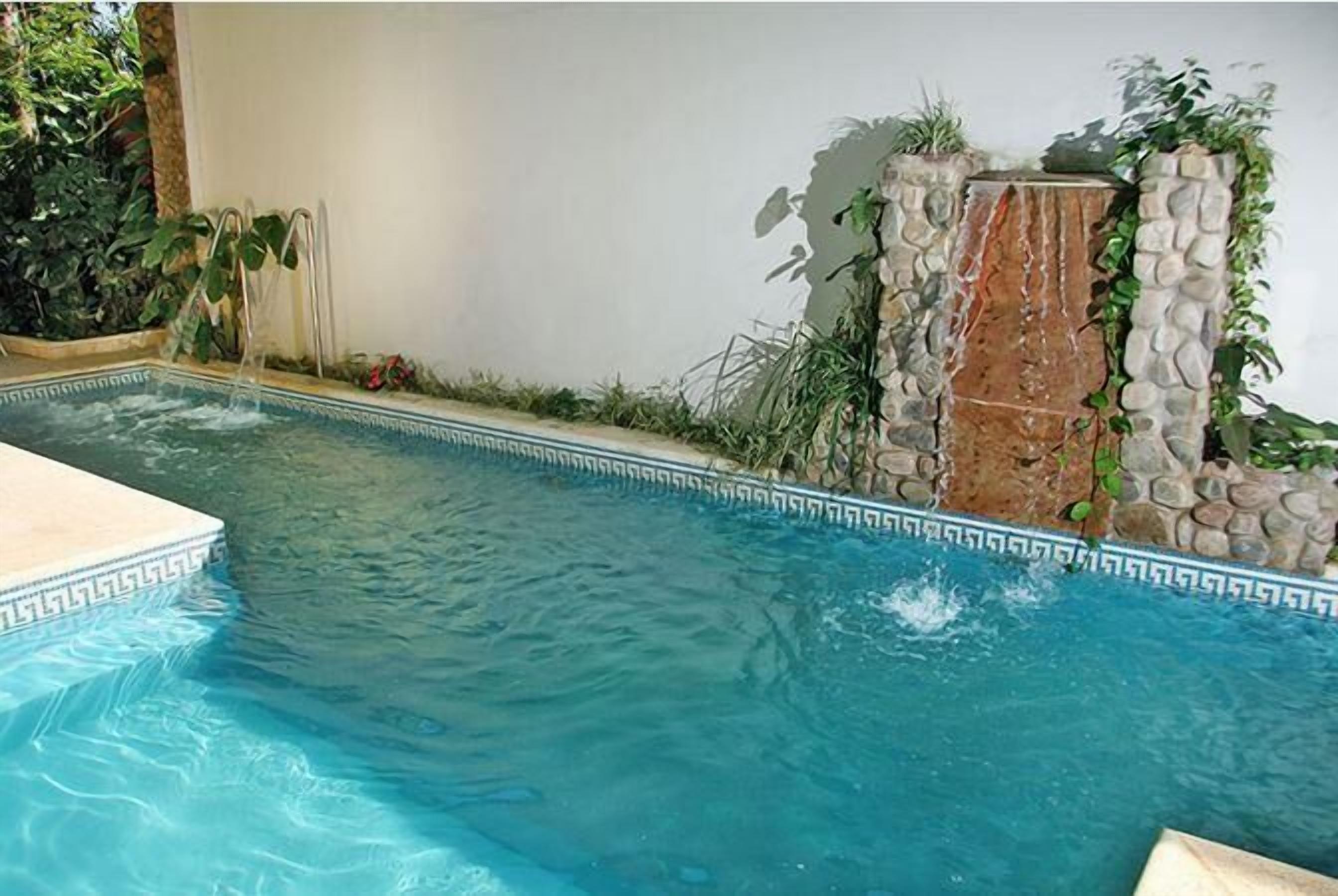 Piscina com cascata de pedra e vegetação ao redor.
