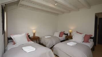 Quarto de hotel com três camas de solteiro, cada uma com travesseiro e mesa de cabeceira com abajur.