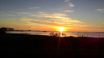 Pôr do sol sobre a água, com uma linha de costa distante e edifícios.