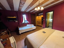 Quarto de hotel com cama, pequena escrivaninha, guarda-roupa e área de chuveiro.
