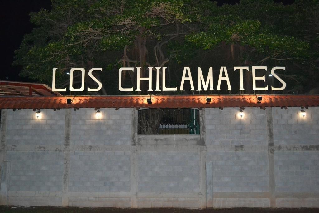 Uma placa com o texto 'LOS CHILAMATES' iluminado contra o céu noturno.