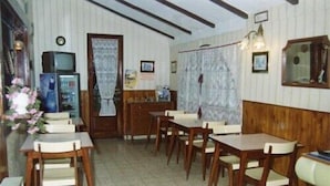 Uma sala de jantar com mesas e cadeiras de madeira, uma televisão e um arranjo floral.