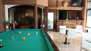 Uma mesa de bilhar com bolas, uma área de refeições com cadeiras e uma cozinha com uma televisão.