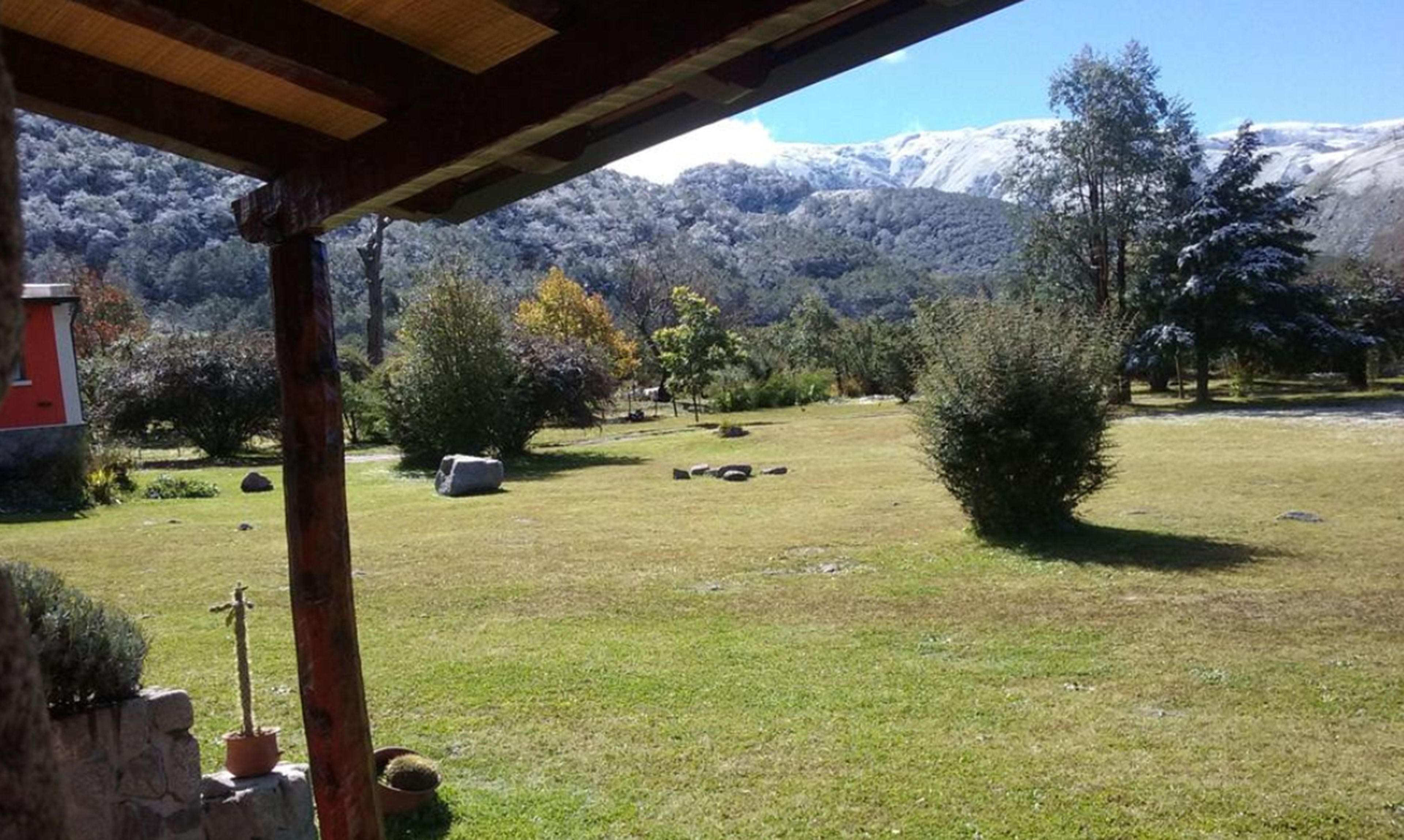 Uma área externa gramada com um muro de pedra, uma pérgola de madeira e vista para montanhas cobertas de neve.
