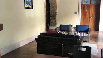 Uma sala de jantar com uma mesa e cadeiras de madeira, um sofá de vime com almofadas e um arco de pedra que dá para uma porta.