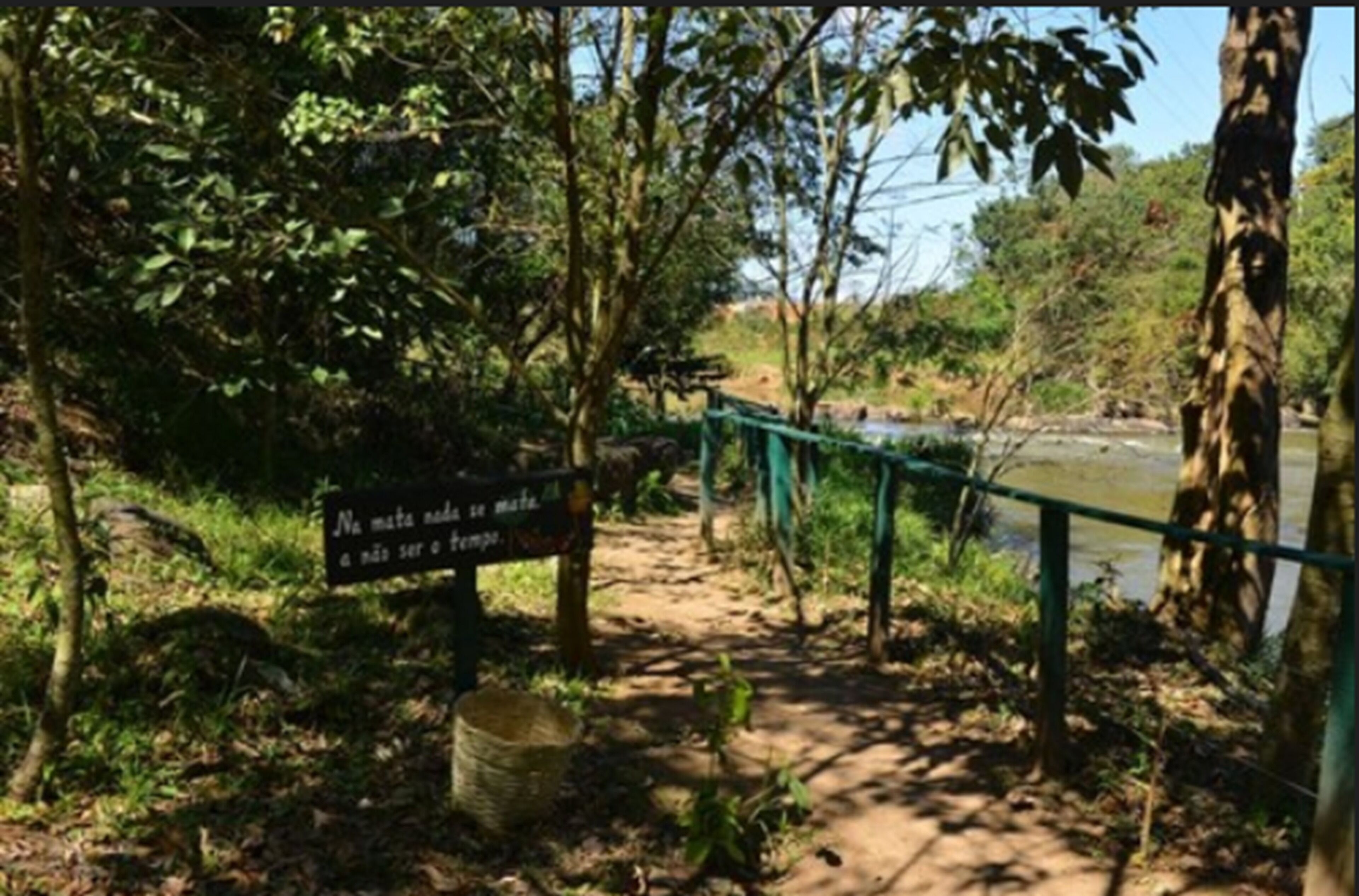 Uma trilha que leva a um rio, com uma placa em idioma estrangeiro.