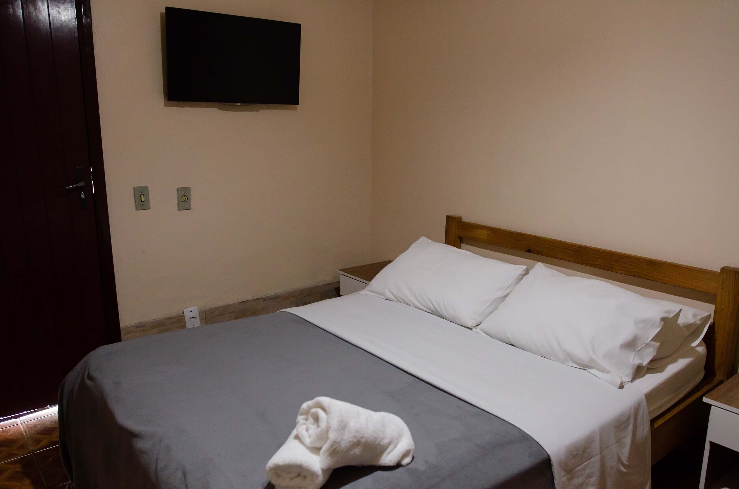 Quarto de hotel com uma cama, uma televisão fixada na parede e uma porta.