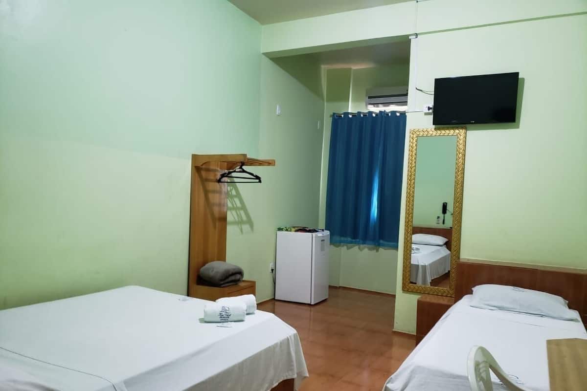 Quarto com duas camas de solteiro, um pequeno frigorífico, um espelho e uma televisão na parede.
