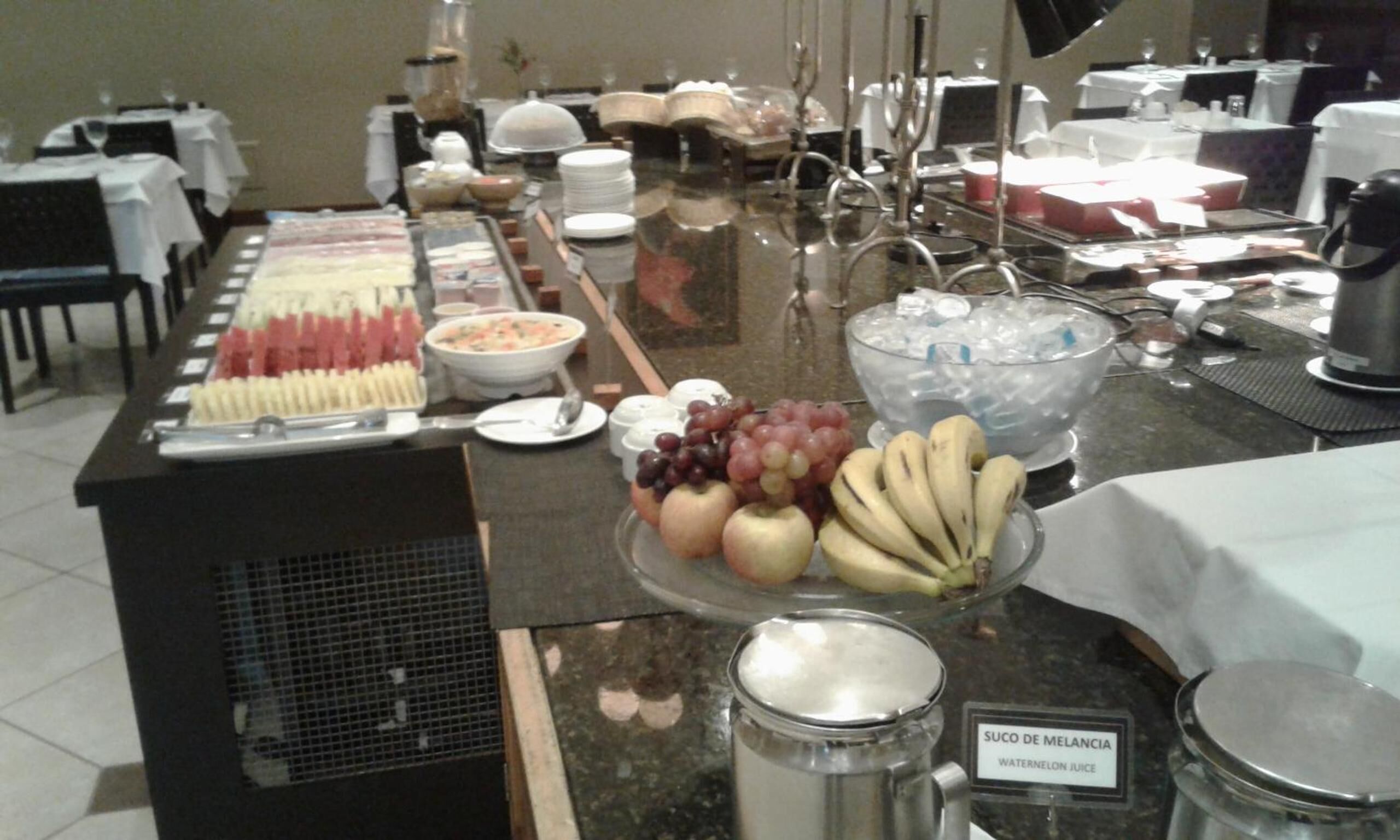 Buffet com diversas opções de comida, incluindo frutas, uma tigela de suco de melancia e um recipiente com suco de melancia.