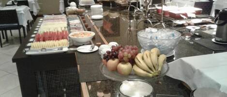 Buffet com diversas opções de comida, incluindo frutas, uma tigela de suco de melancia e um recipiente com suco de melancia.