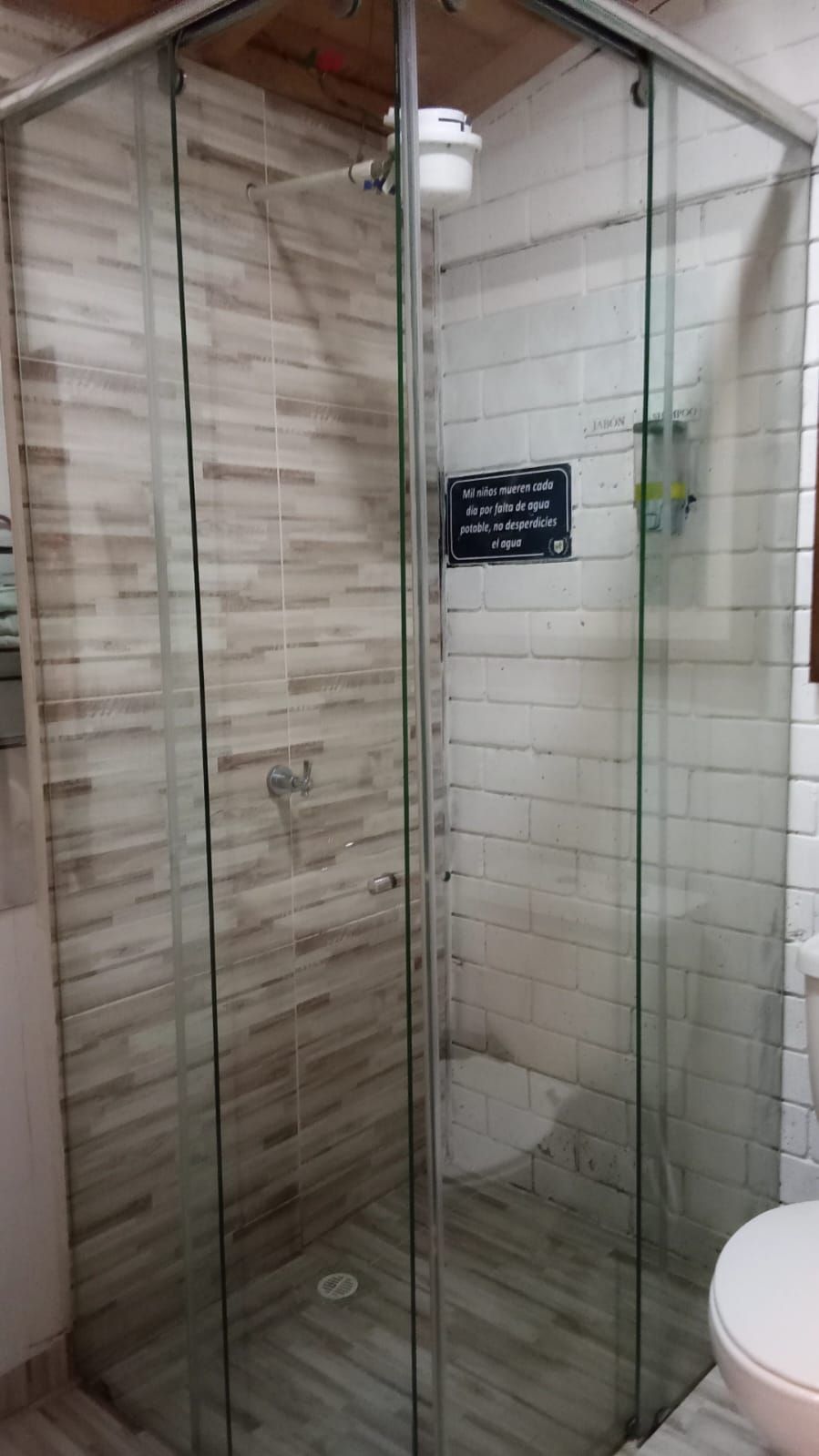 Um chuveiro envidraçado com parede azulejada e uma placa em espanhol.