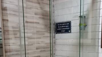 Um chuveiro envidraçado com parede azulejada e uma placa em espanhol.
