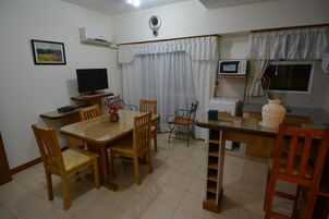Uma sala de jantar com mesa e cadeiras de madeira, uma televisão e um micro-ondas.