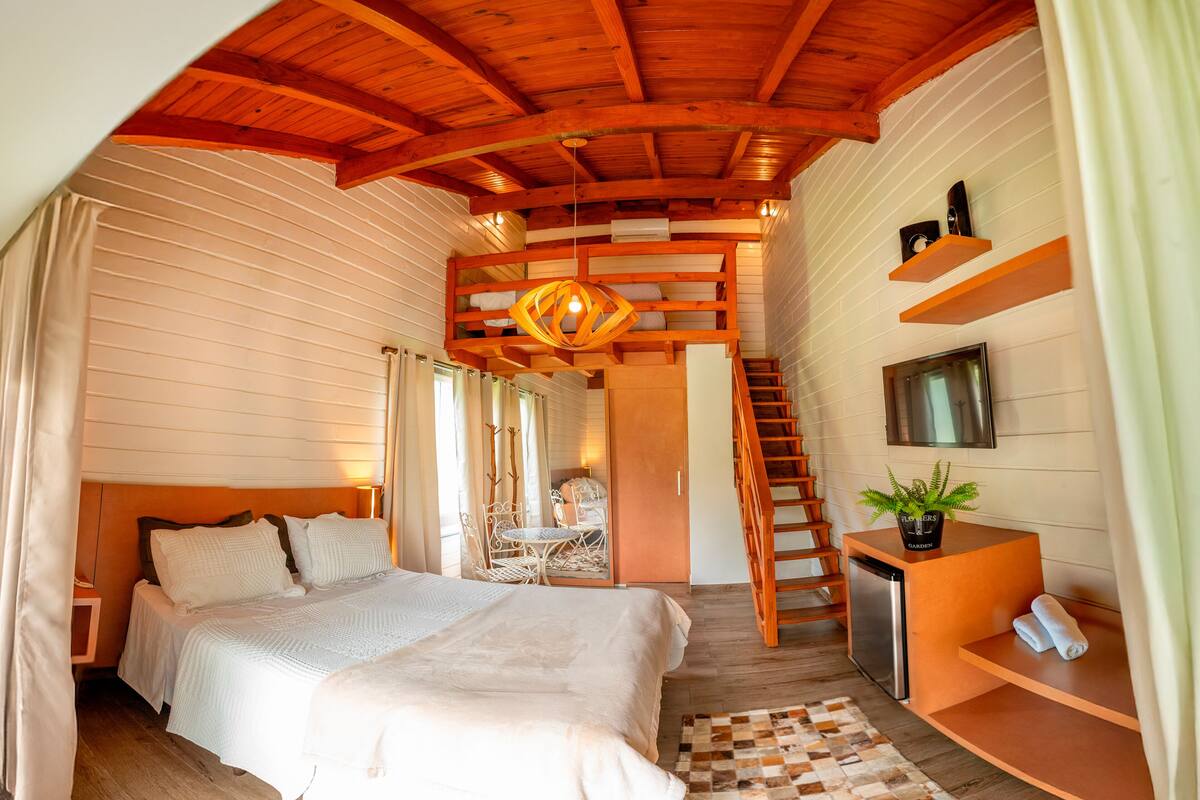 Um quarto com uma cama, uma escrivaninha, uma cadeira, uma televisão, uma escada e um espelho.