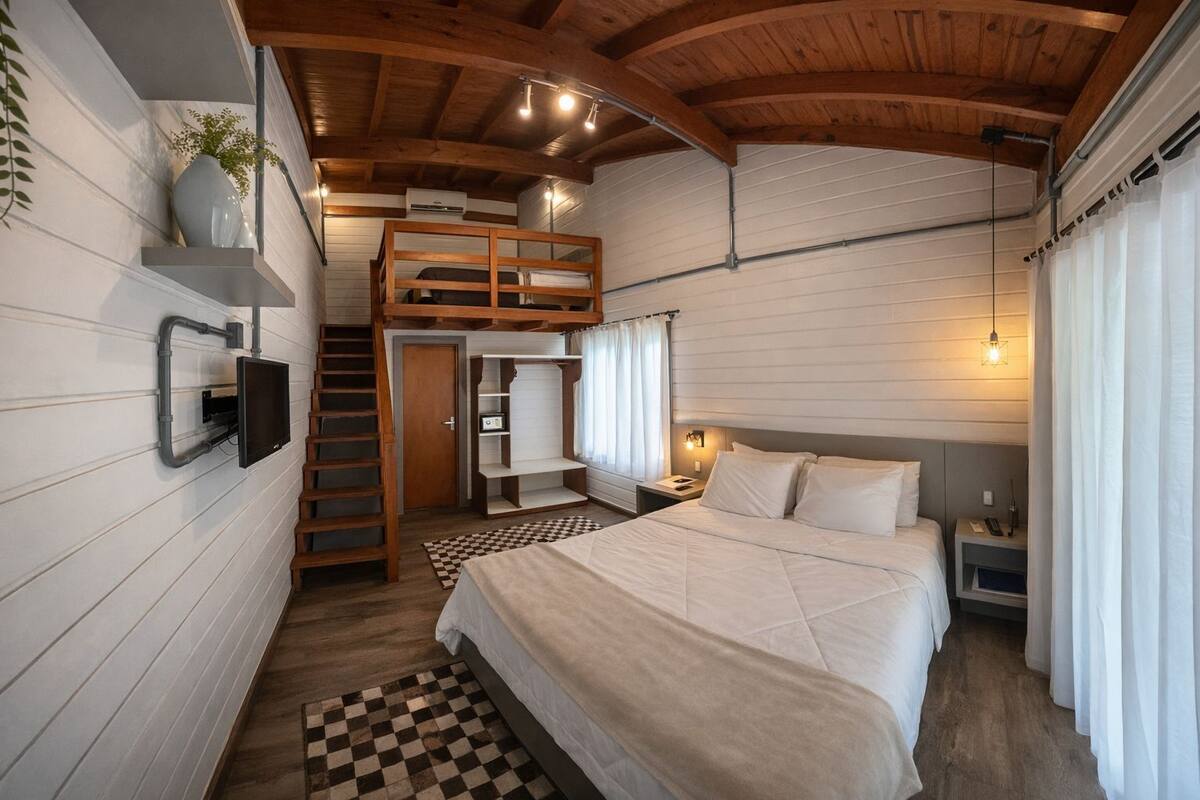 Quarto com uma cama beliche, televisão, escrivaninha e escada.