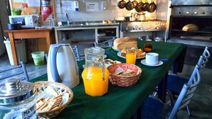 Uma mesa com disposição para café da manhã, incluindo pão, suco e uma cafeteira.