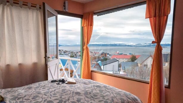 Quarto com uma grande janela que oferece vista para uma cidade costeira e montanhas.