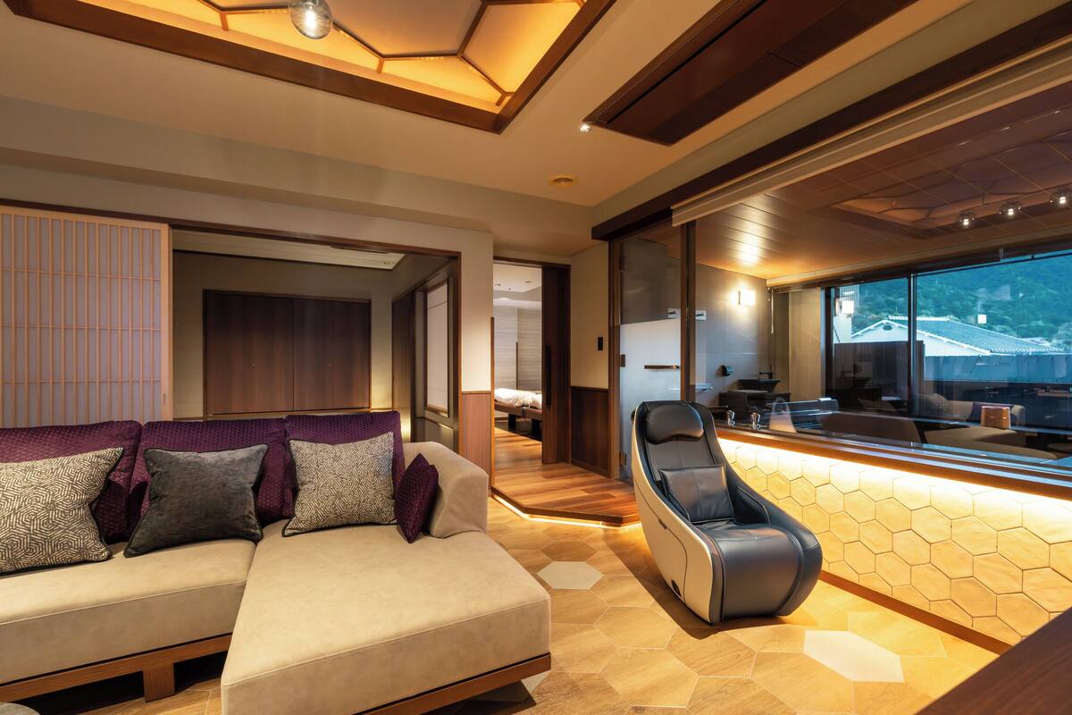 Uma sala de estar moderna com sofá, poltrona de massagem e vista para o exterior por grandes janelas.