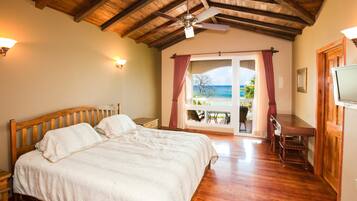Quarto com teto de madeira, uma cama, uma escrivaninha e vista para o mar pela janela.