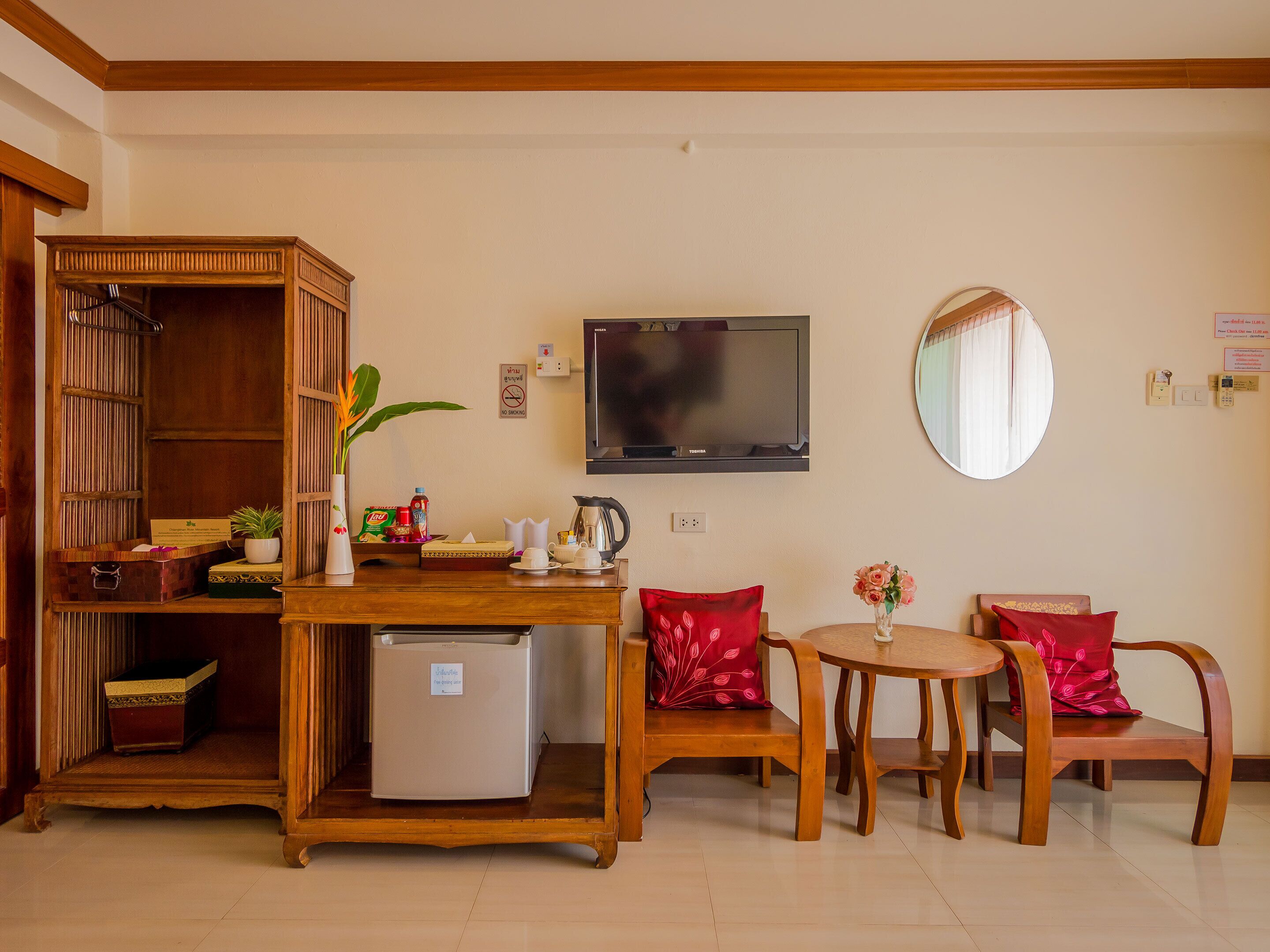 Quarto de hotel com secretária de madeira, televisão, mini-frigorífico e área de estar com duas cadeiras e uma mesa.