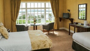 Quarto de hotel com duas camas, uma escrivaninha, uma cadeira, televisão e vista para o exterior.