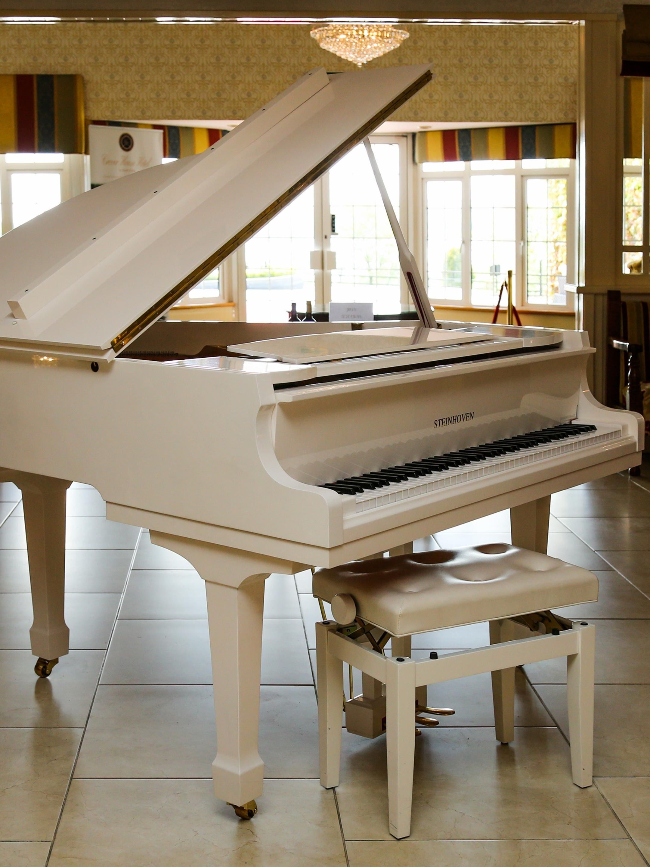 Um piano de cauda imponente em uma sala ampla com janelas grandes e um candelabro.