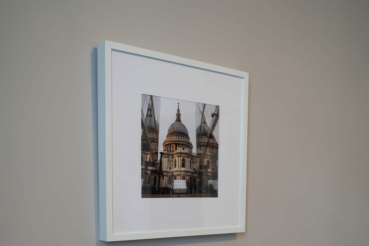 Uma fotografia emoldurada de um edifício numa parede, uma pequena mesa com uma planta e uma cadeira.