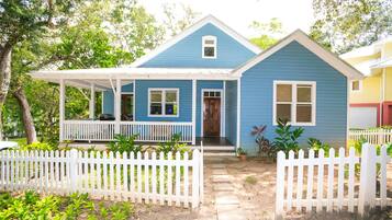 Uma casa de dois andares com fachada azul, varanda branca e cerca branca de piquete.