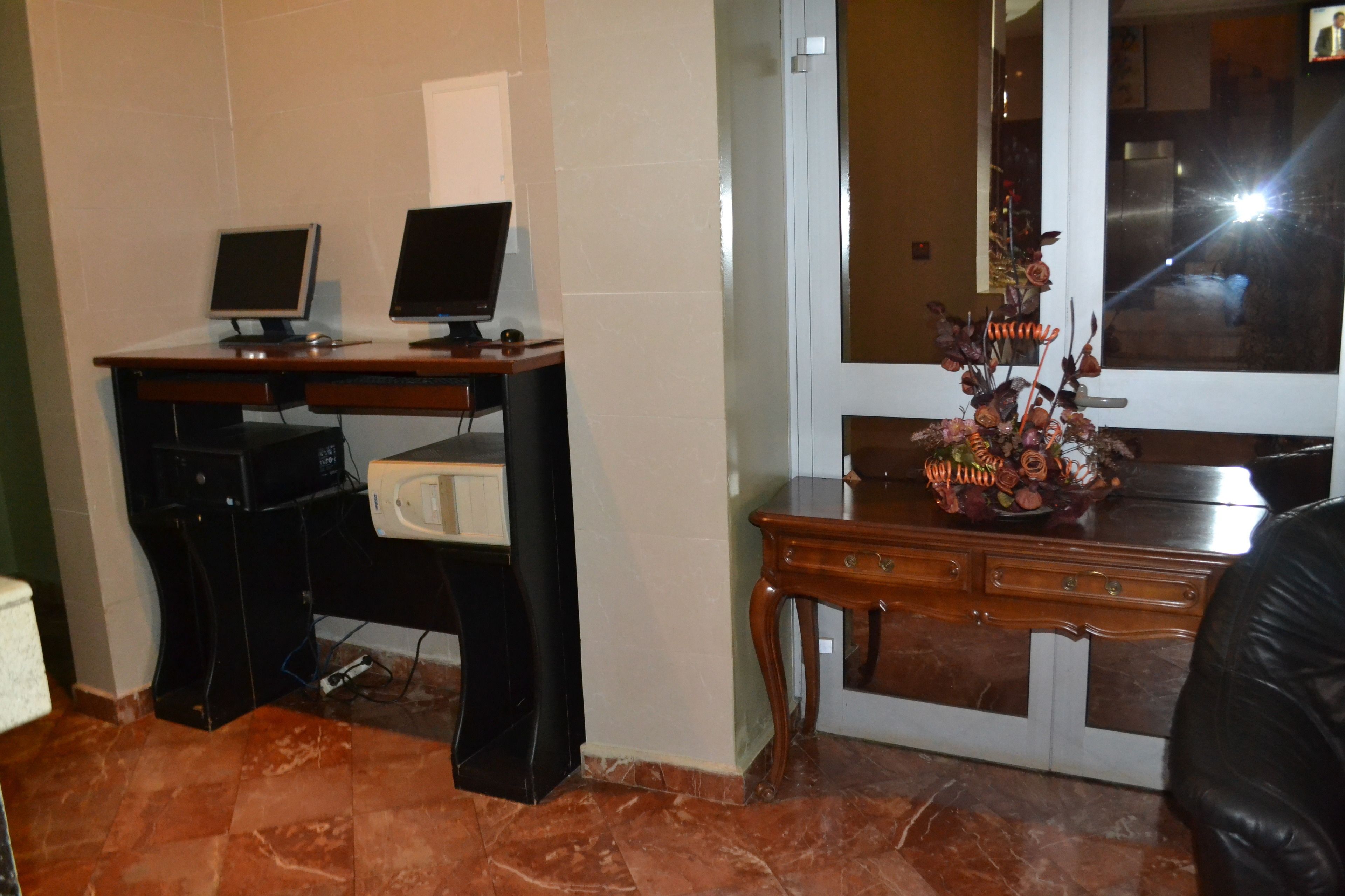 Quarto com escrivaninha, dois monitores, micro-ondas, armário e um vaso decorativo.