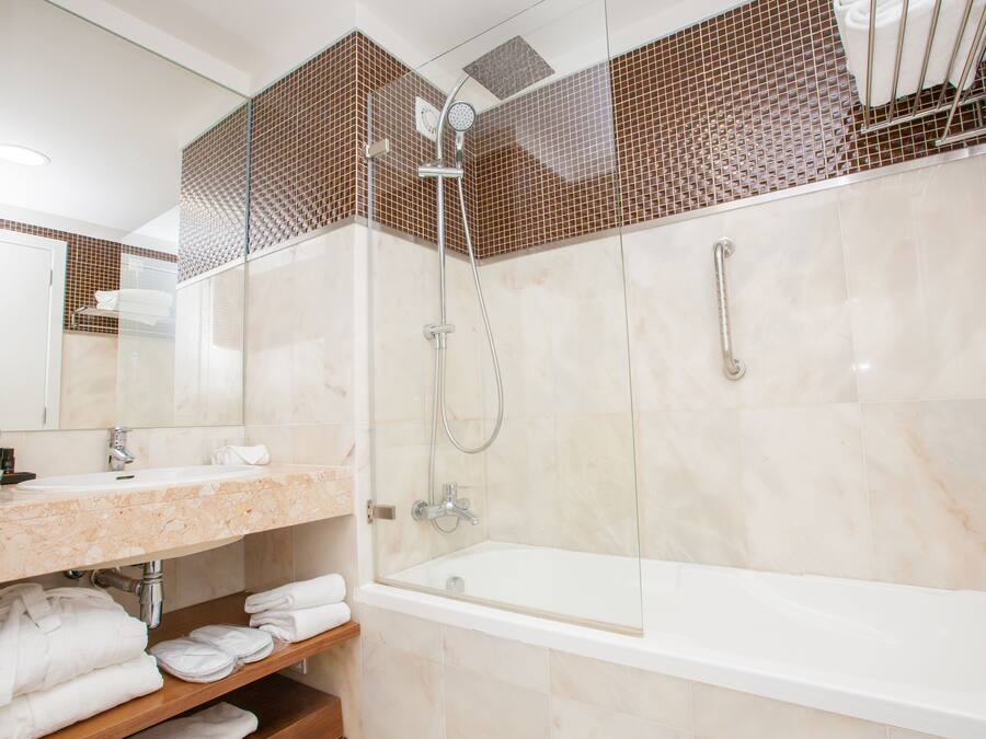 Uma casa de banho moderna com cabine de duche em vidro, lavatório branco e toucador em azulejos de mármore.