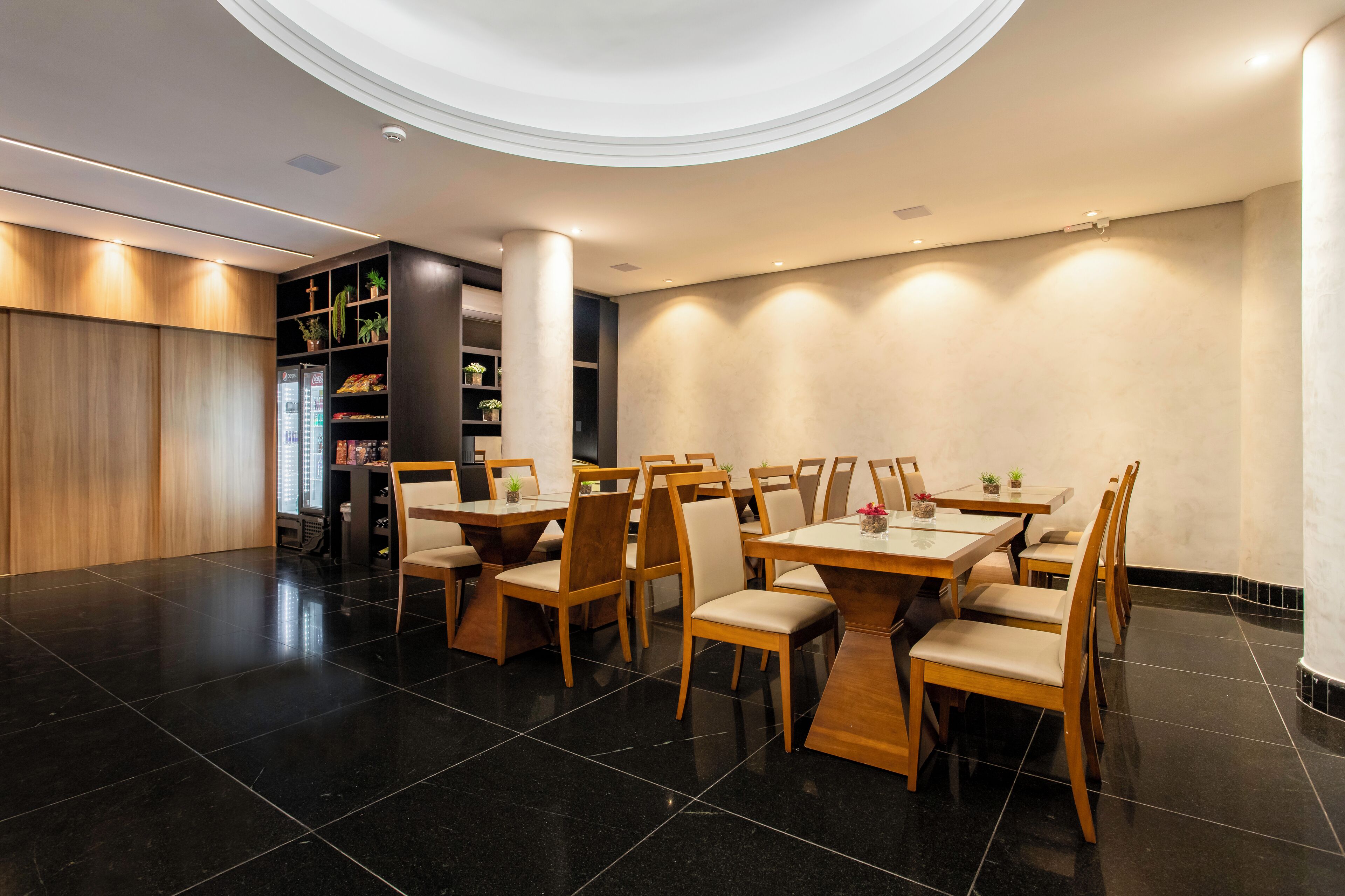 Uma sala de jantar moderna com pisos em azulejos pretos, mesas e cadeiras de madeira e um pilar central.